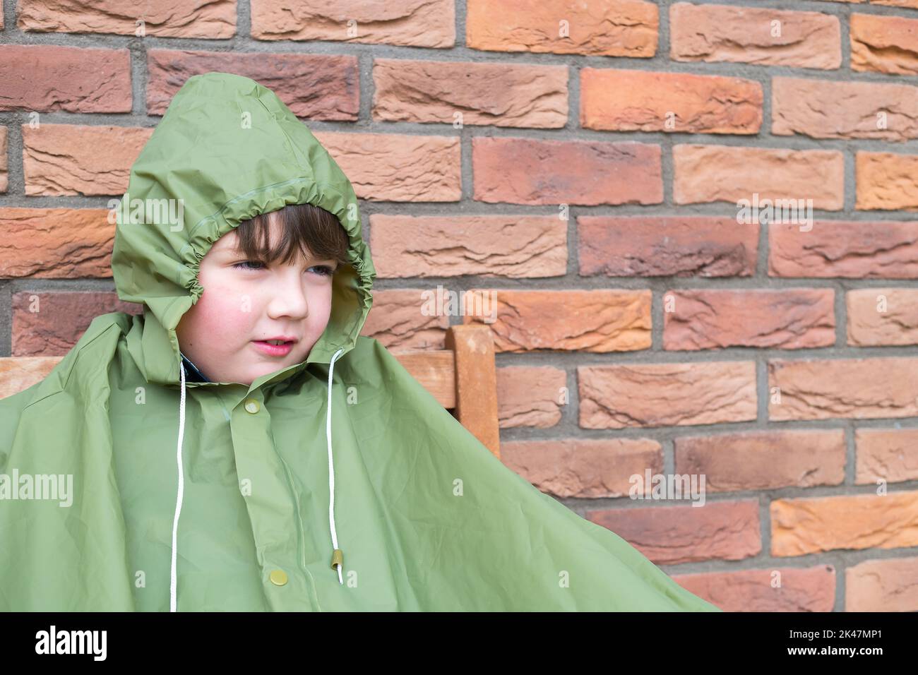 Child, boy in the green raincoat is sitting and waiting for stop ...