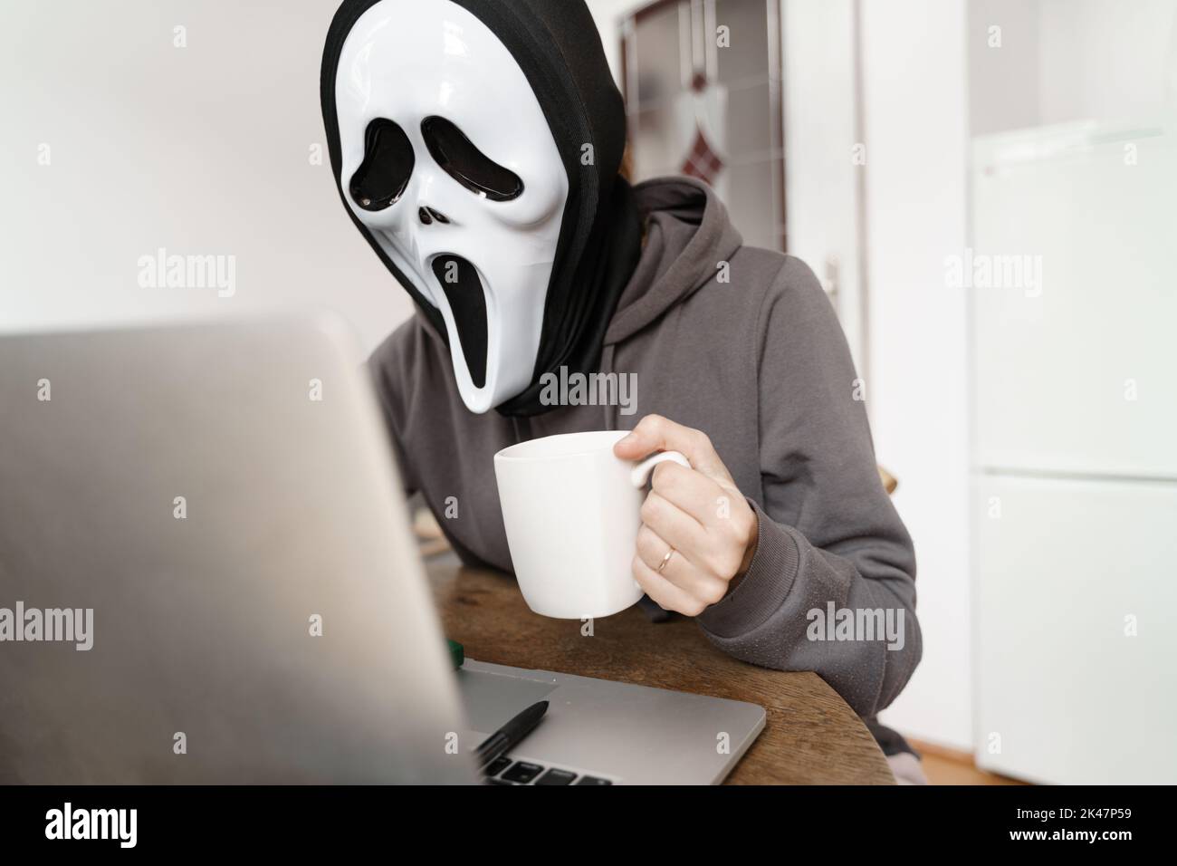 Anonymus person with ghost mask working with laptop. Halloween work ...