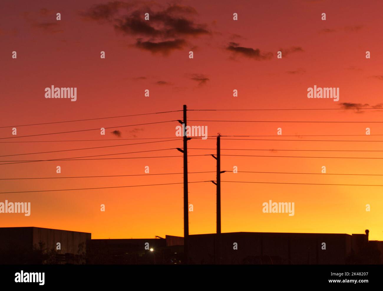 a power line with industrial buildings underneath during a fiery sunset ...