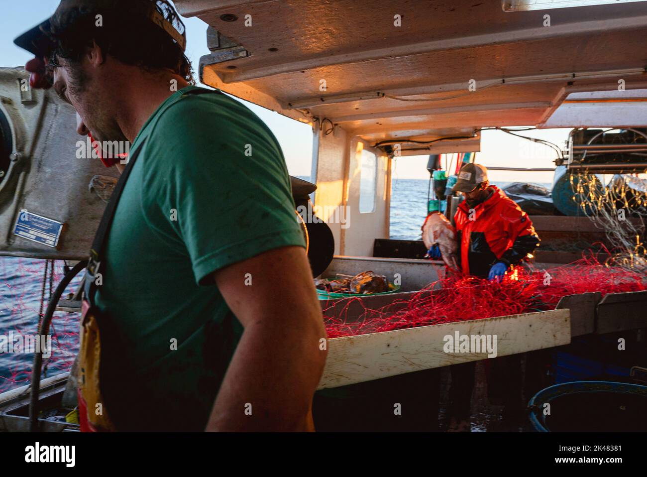 At dusk, a crew member on a commercial fishing boat takes a break from ...