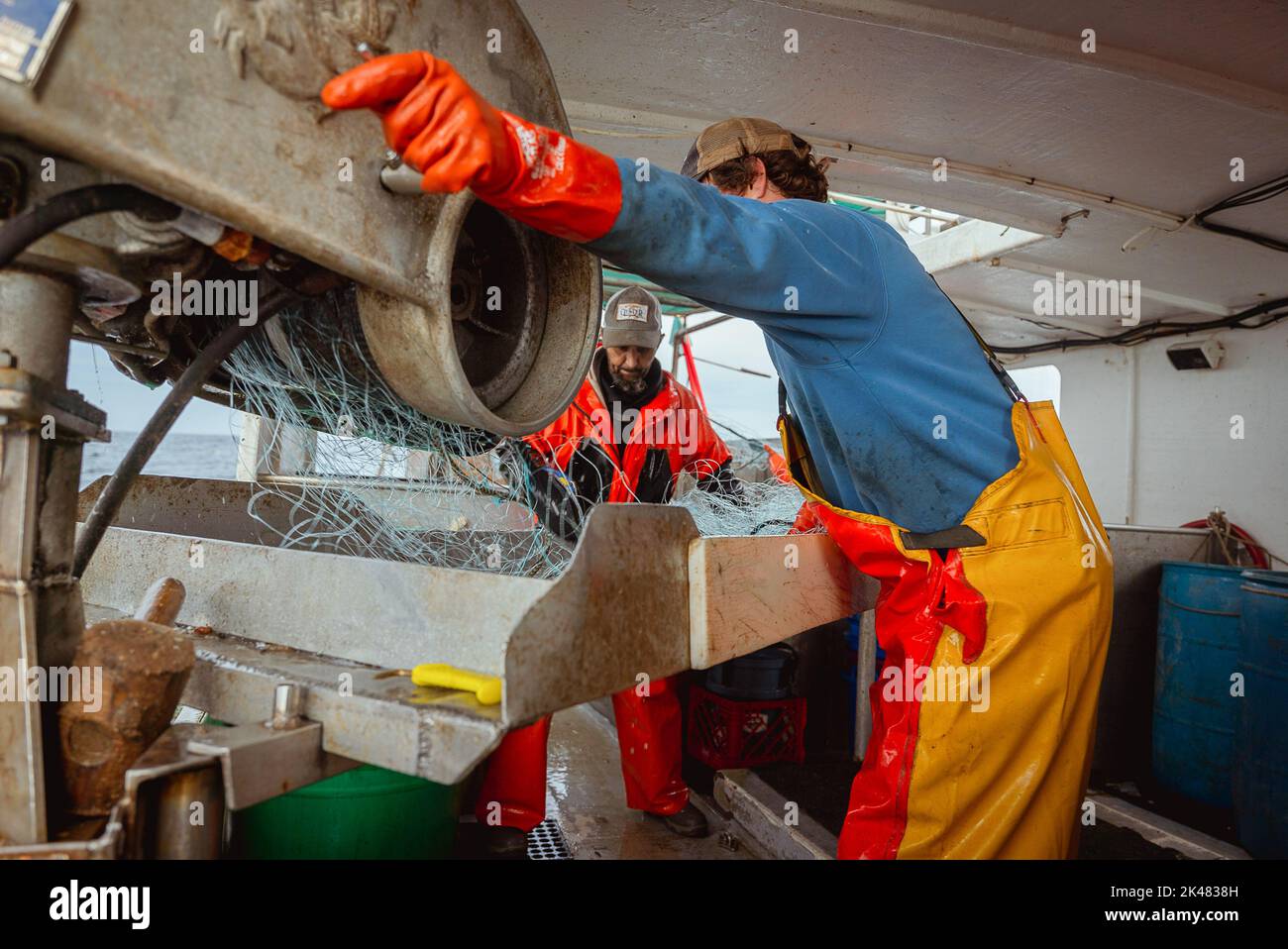A crew member aboard a commercial fishing boat cranks the lever of a ...