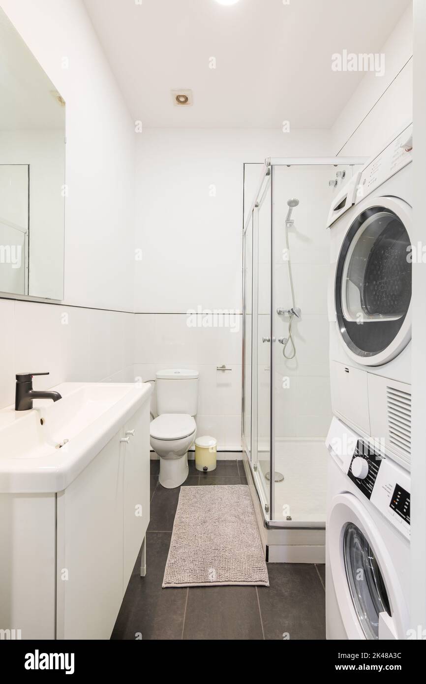 Small and narrow white bathroom with shower cabin, washing machine and ...