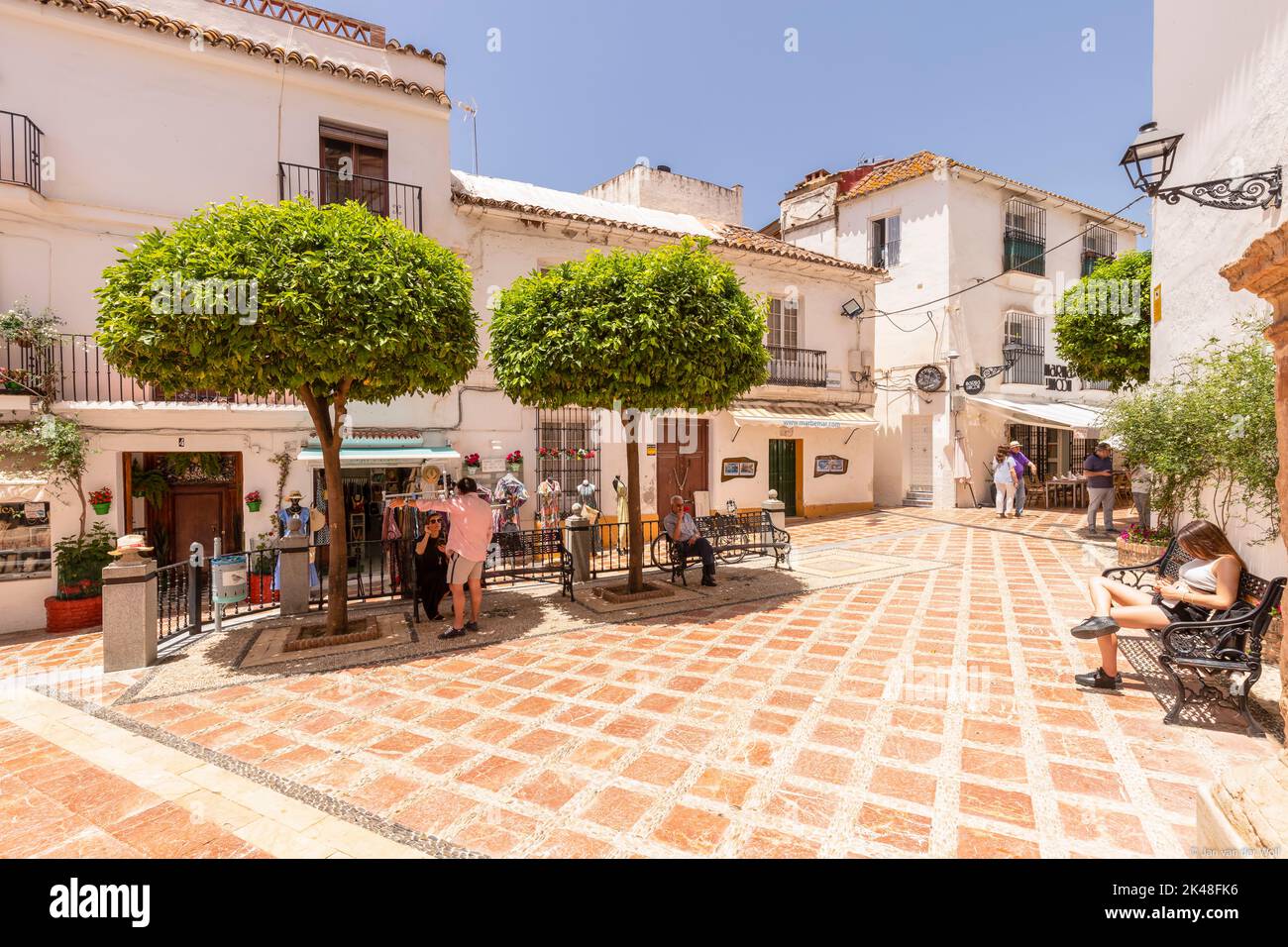 People walk and sit on a bench on a small square in the cozy ...