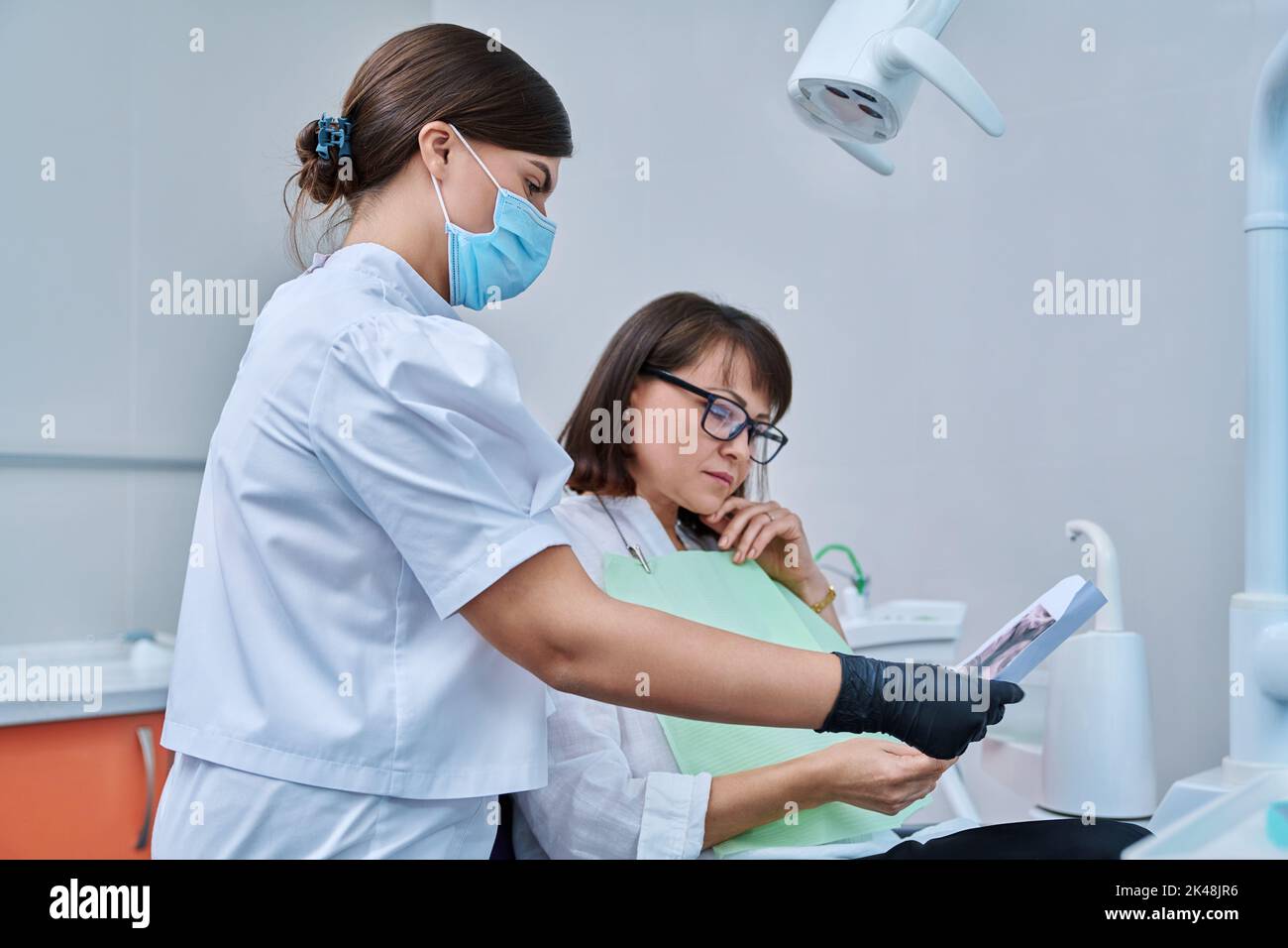 Female dentist talking to woman patient, discussing x-rays of teeth and ...