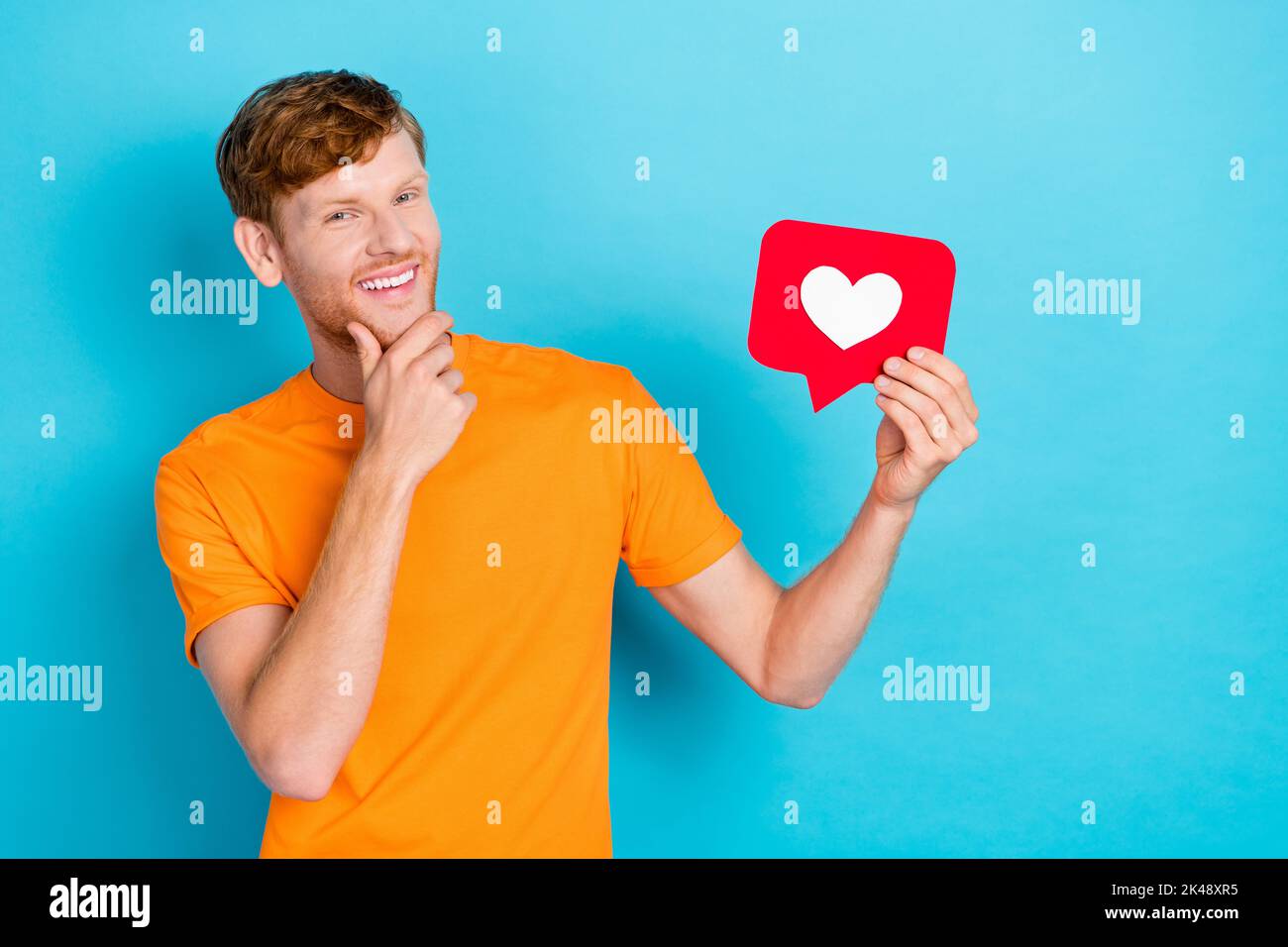 Photo of positive clever man wear orange t-shirt arm chin holding heart ...