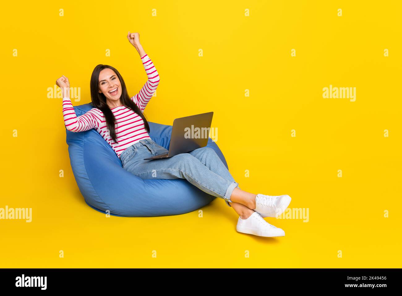 Full size photo of cheerful girl striped shirt jeans sit in pouf with ...