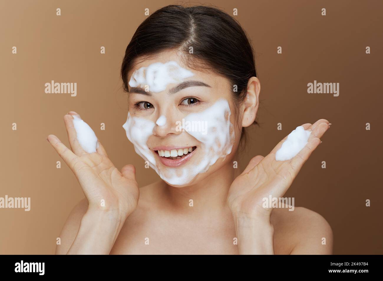 Portrait of young woman washing face on beige background Stock Photo ...