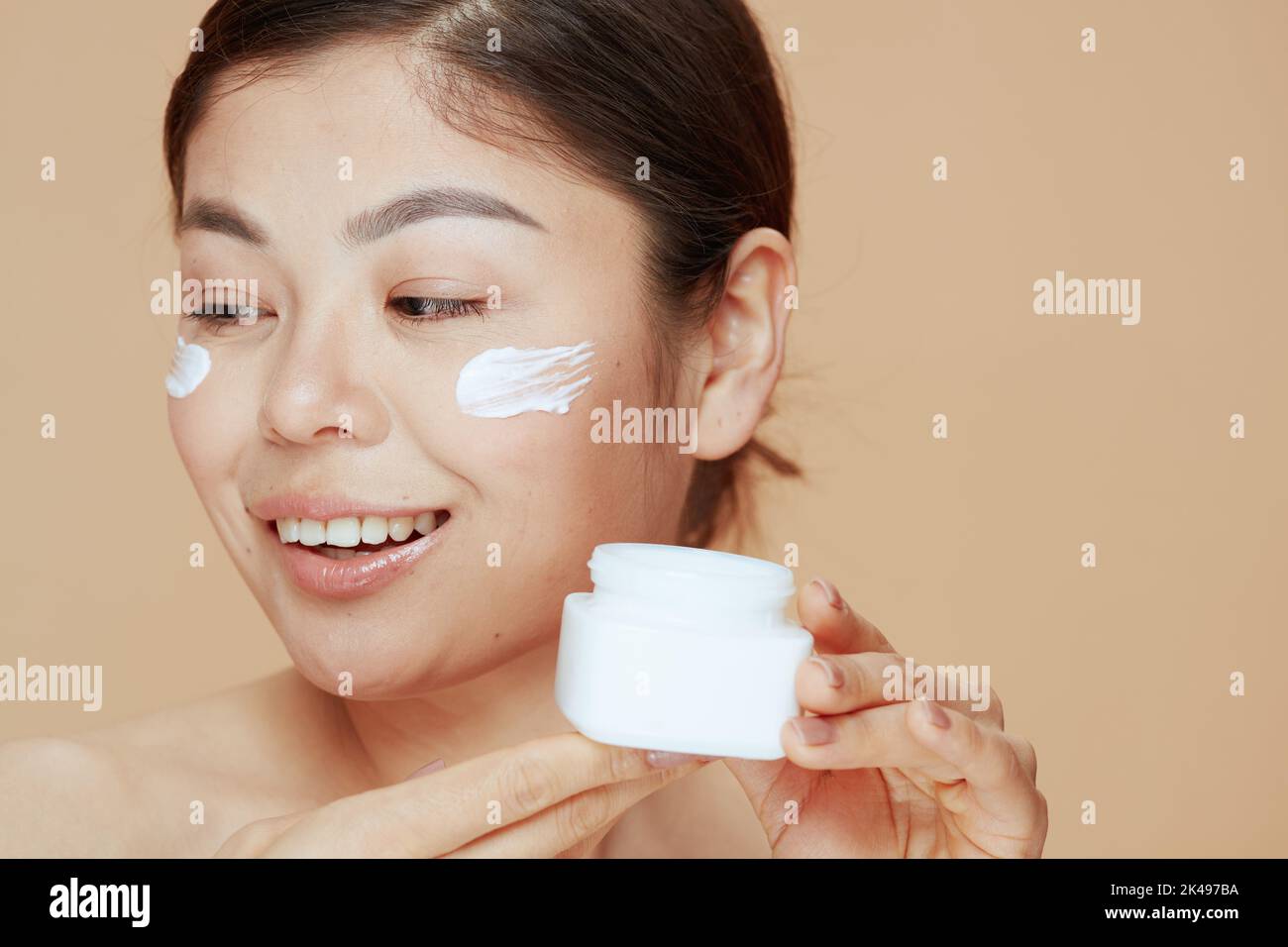 modern asian woman with facial cream jar and facial cream on face against beige background Stock ...