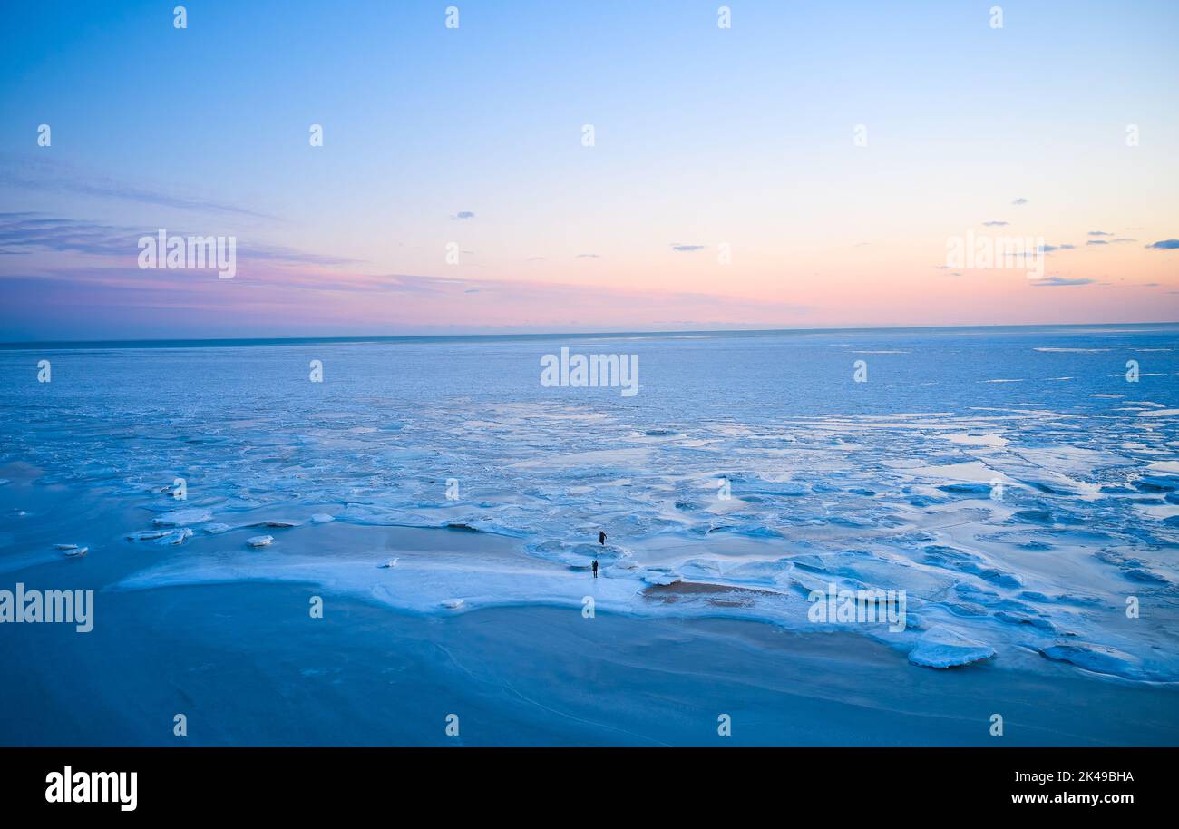 Aerial view - two people walk on ice on sunset over the frozen sea ...