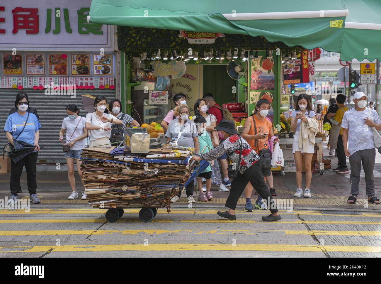 A cardboard collector passes by people waiting for the traffic light in ...