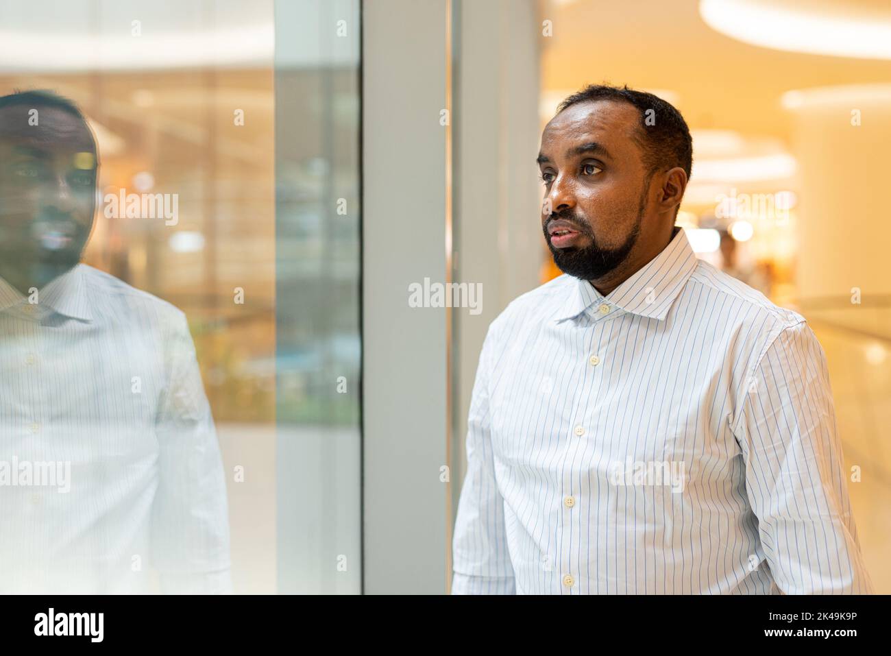 Black man looking through window while thinking Stock Photo - Alamy