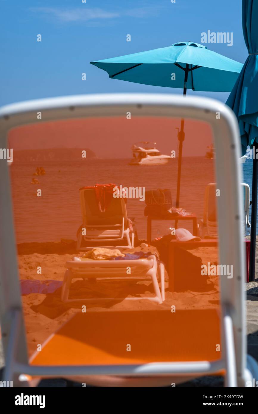 beach scene with orange sun lounger, blue sun shade and boat on Sunj ...