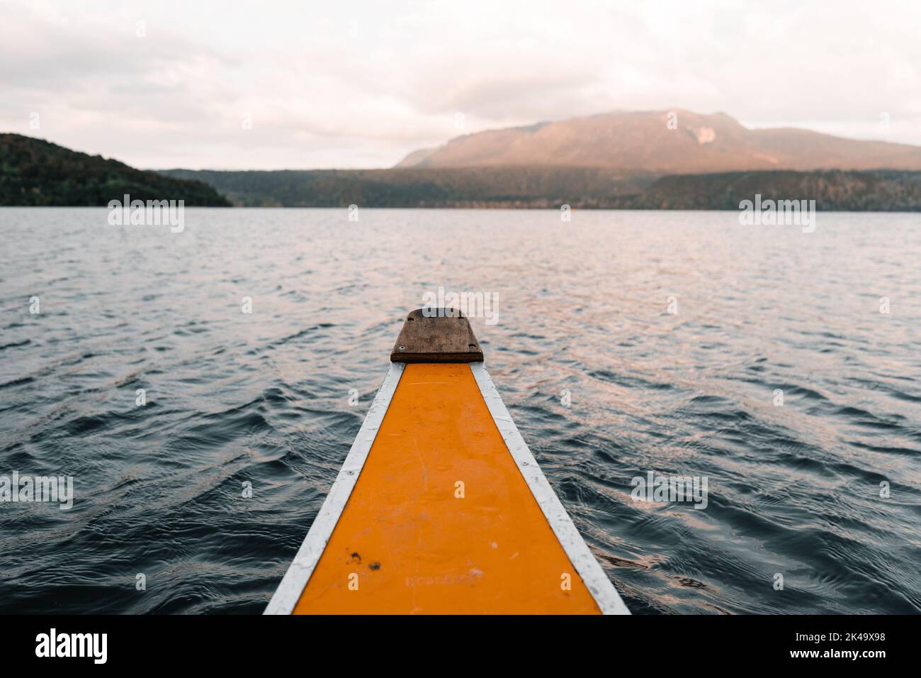 pointed bow of a white and orange wooden kayak heading to the leafy ...