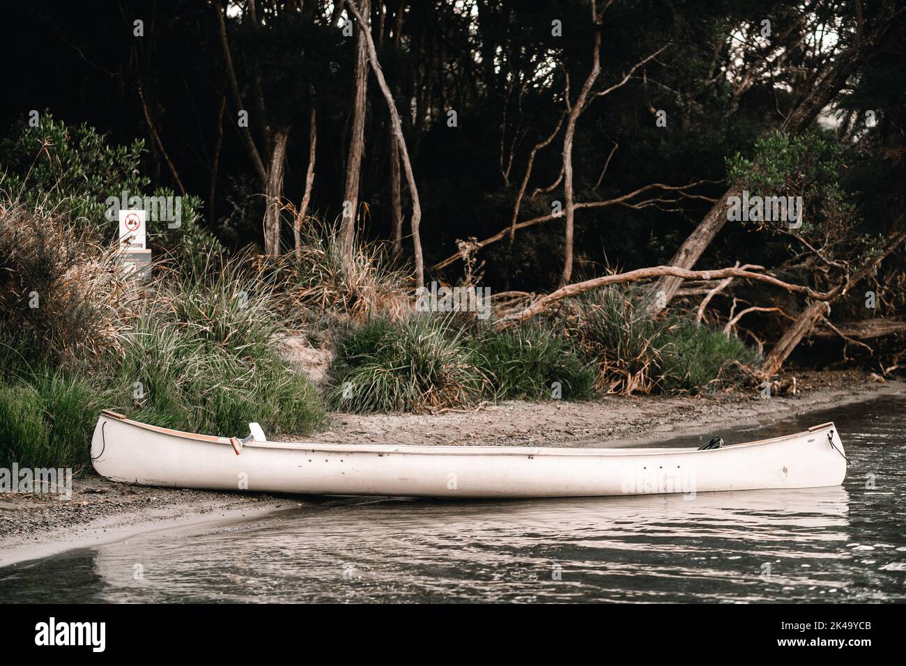 white wooden kayak with the bow in the water and the stern on the sand ...