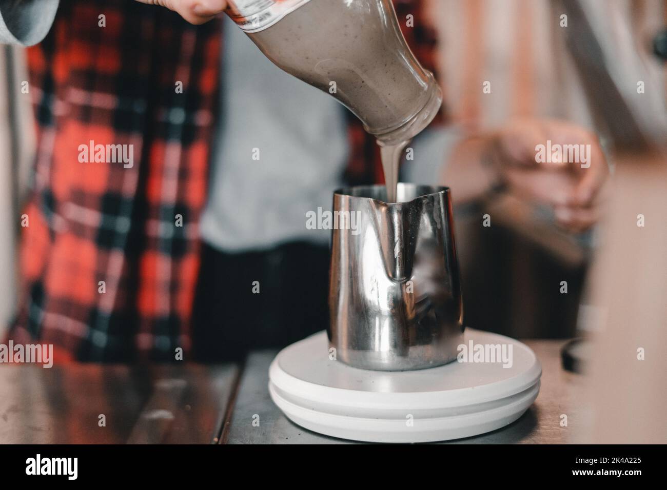 creamy liquid chocolate pouring from a glass bottle into a clean metal ...