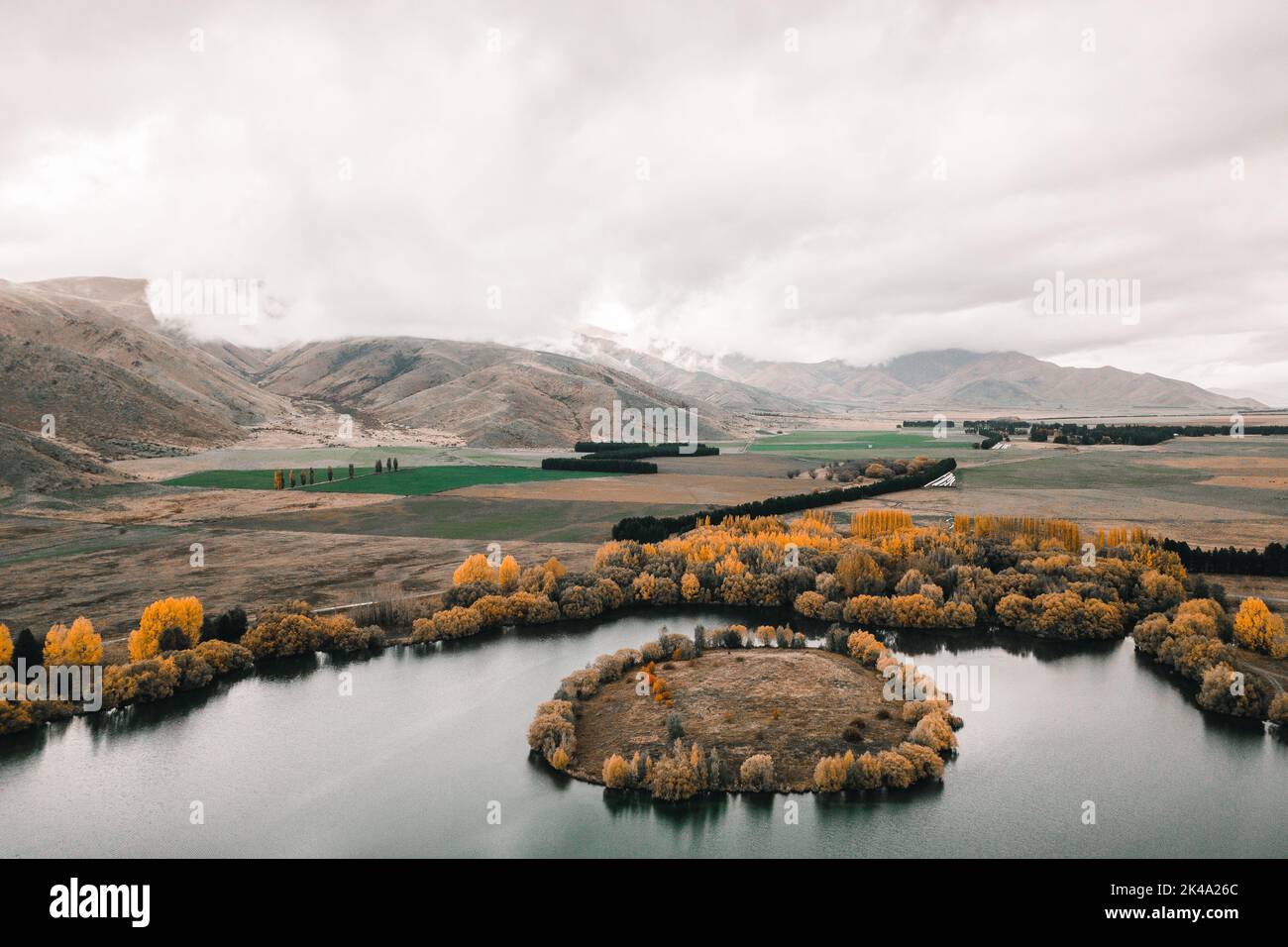 large plain with farm fields near small lake island among desolate mist ...