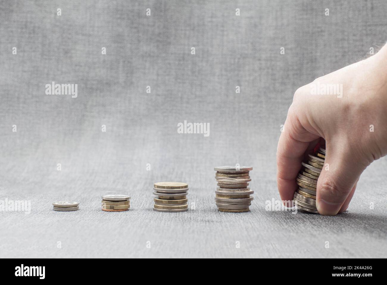 A hand picking up old coins arranged in stacks in a gray background ...