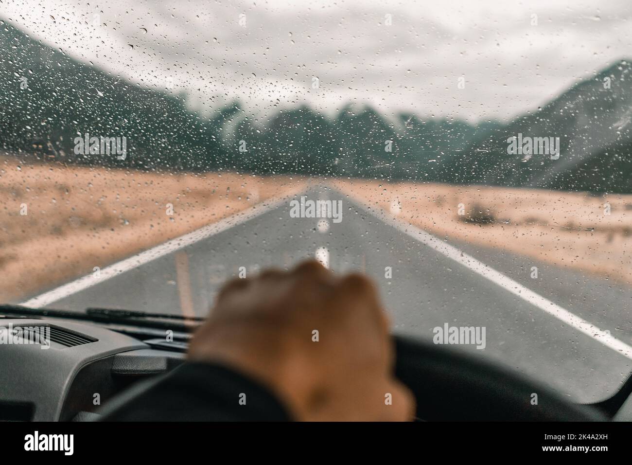 left hand of caucasian boy on the steering wheel of a van moving on a straight road between the ...