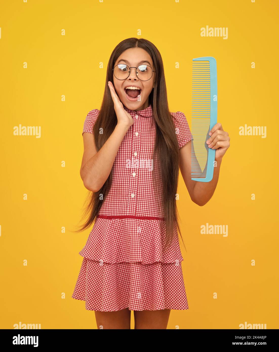 Child brushing combing hair with big comb on yellow isolated studio ...