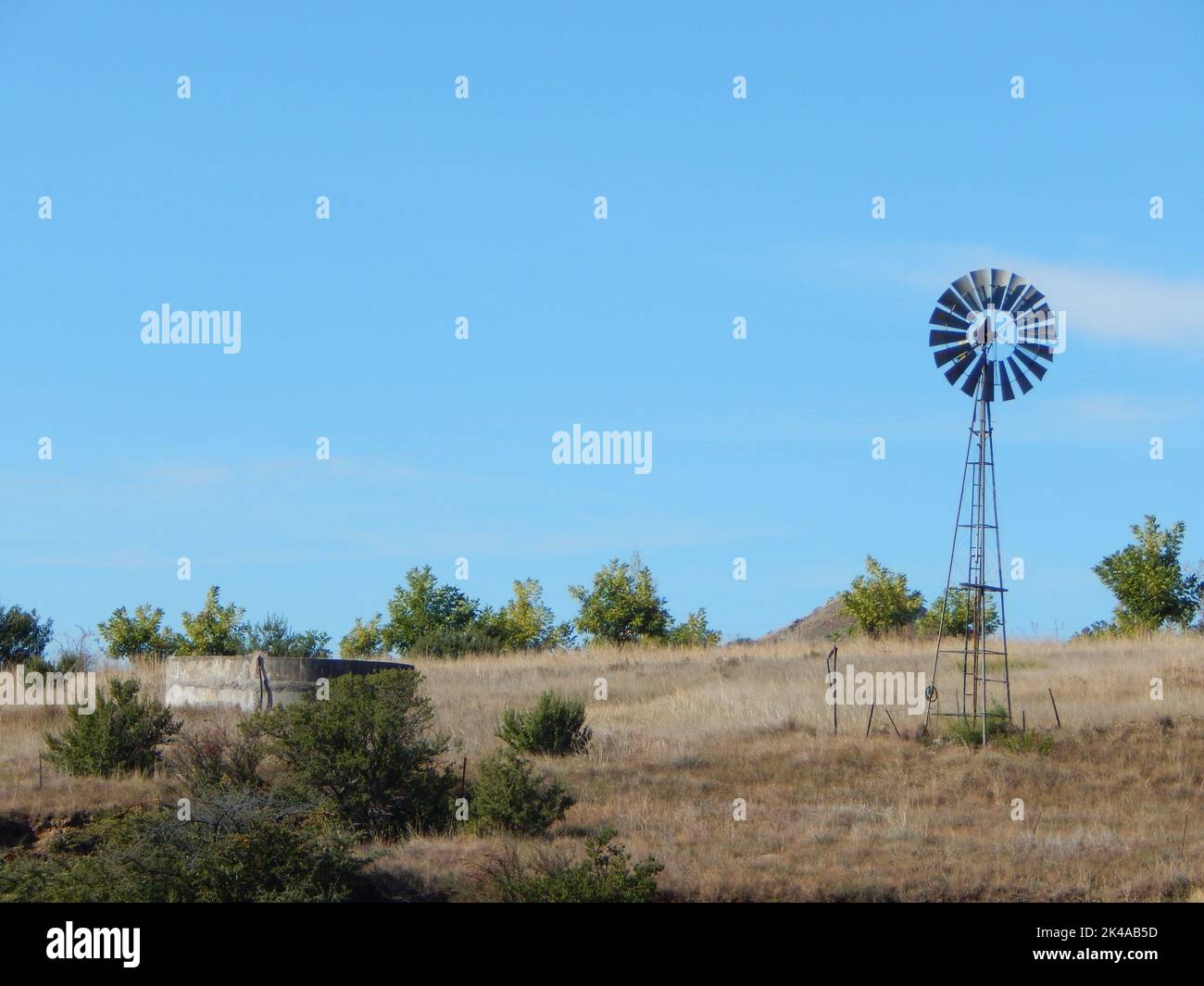 A low-angle shot of a black windmill in the valley with some trees ...