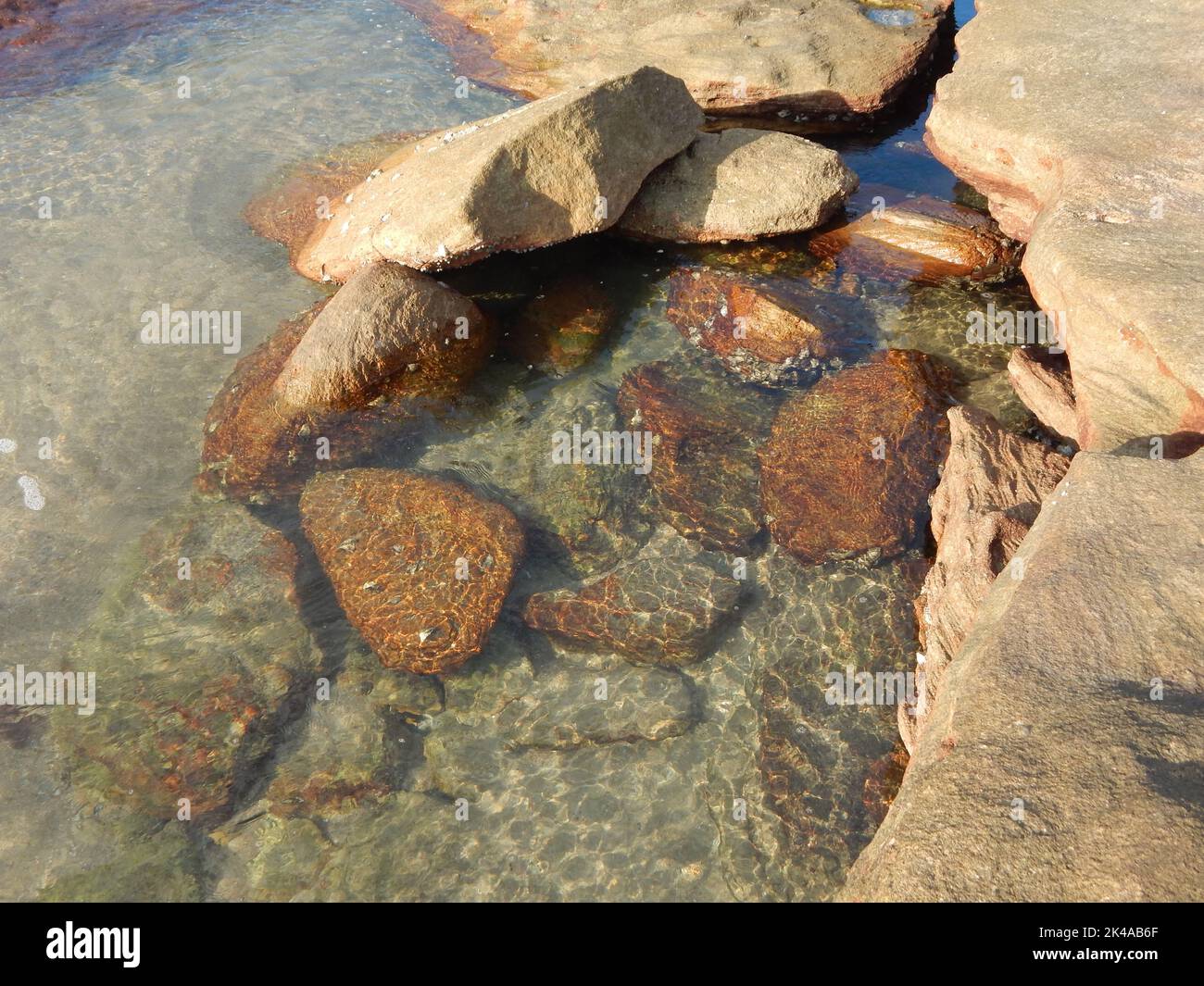 A closeup of a pile of beach stones in the water, sunlight on them ...