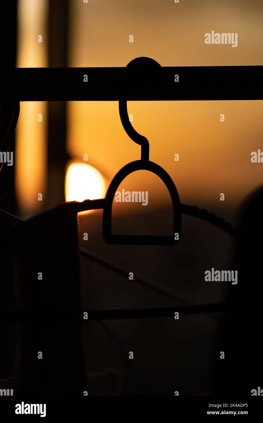 A vertical shot of the silhouettes of clothes hangers on a metal bar ...