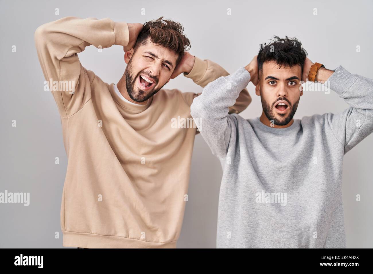 Young homosexual couple standing over white background crazy and scared ...