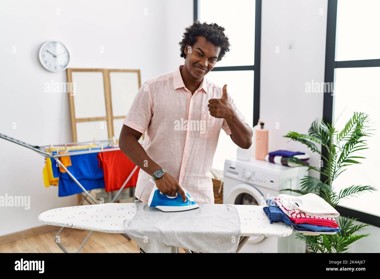 African man with curly hair ironing clothes at home doing happy thumbs ...
