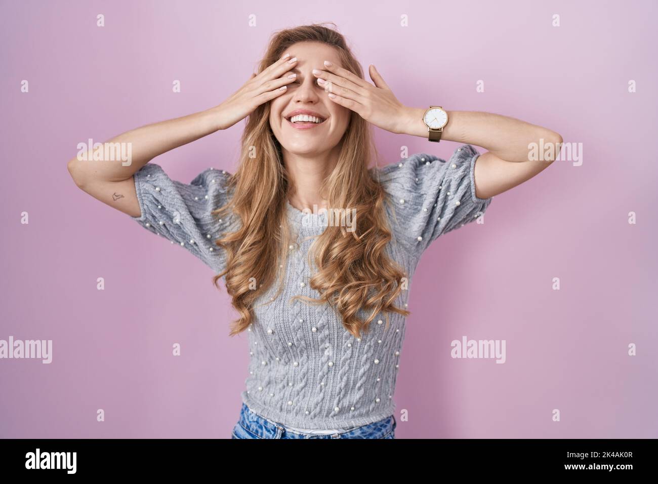 Beautiful blonde woman standing over pink background covering eyes with ...
