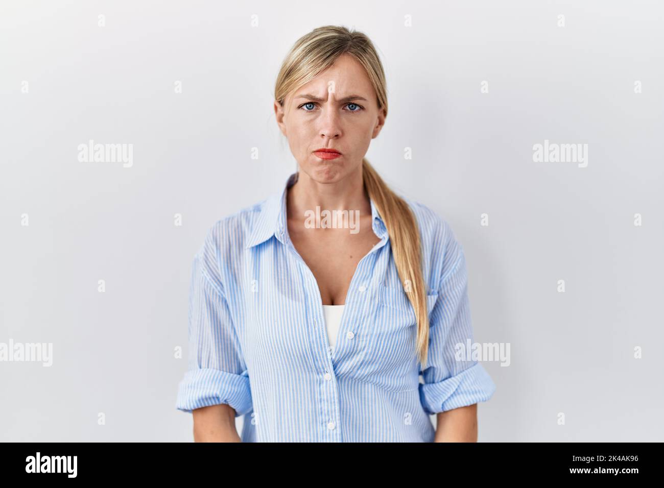 Beautiful blonde woman standing over white background skeptic and ...