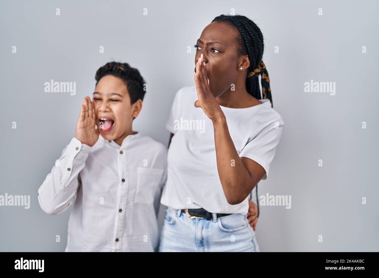 Young mother and son standing together over white background shouting ...