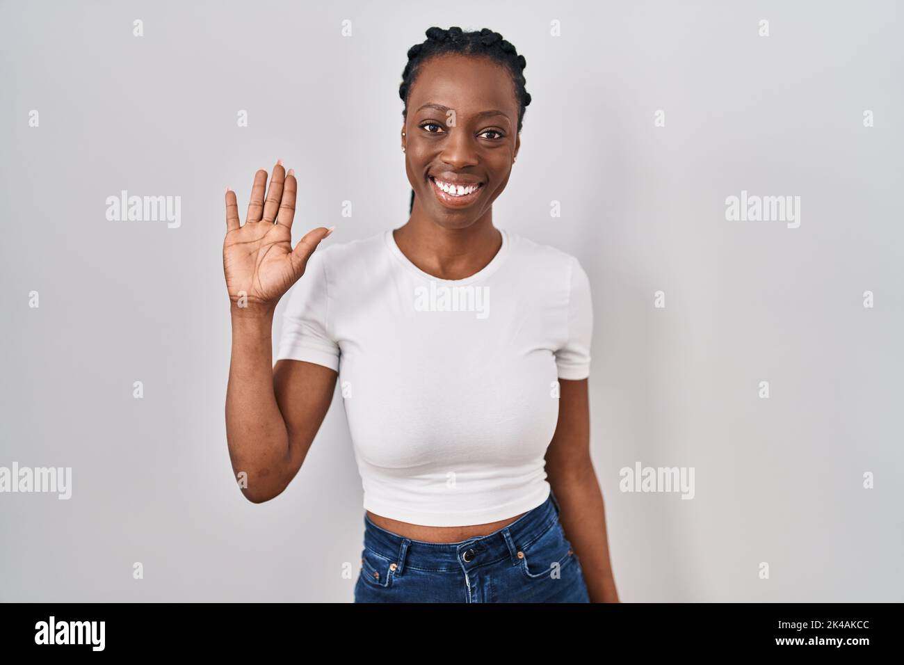 Beautiful black woman standing over isolated background waiving saying ...
