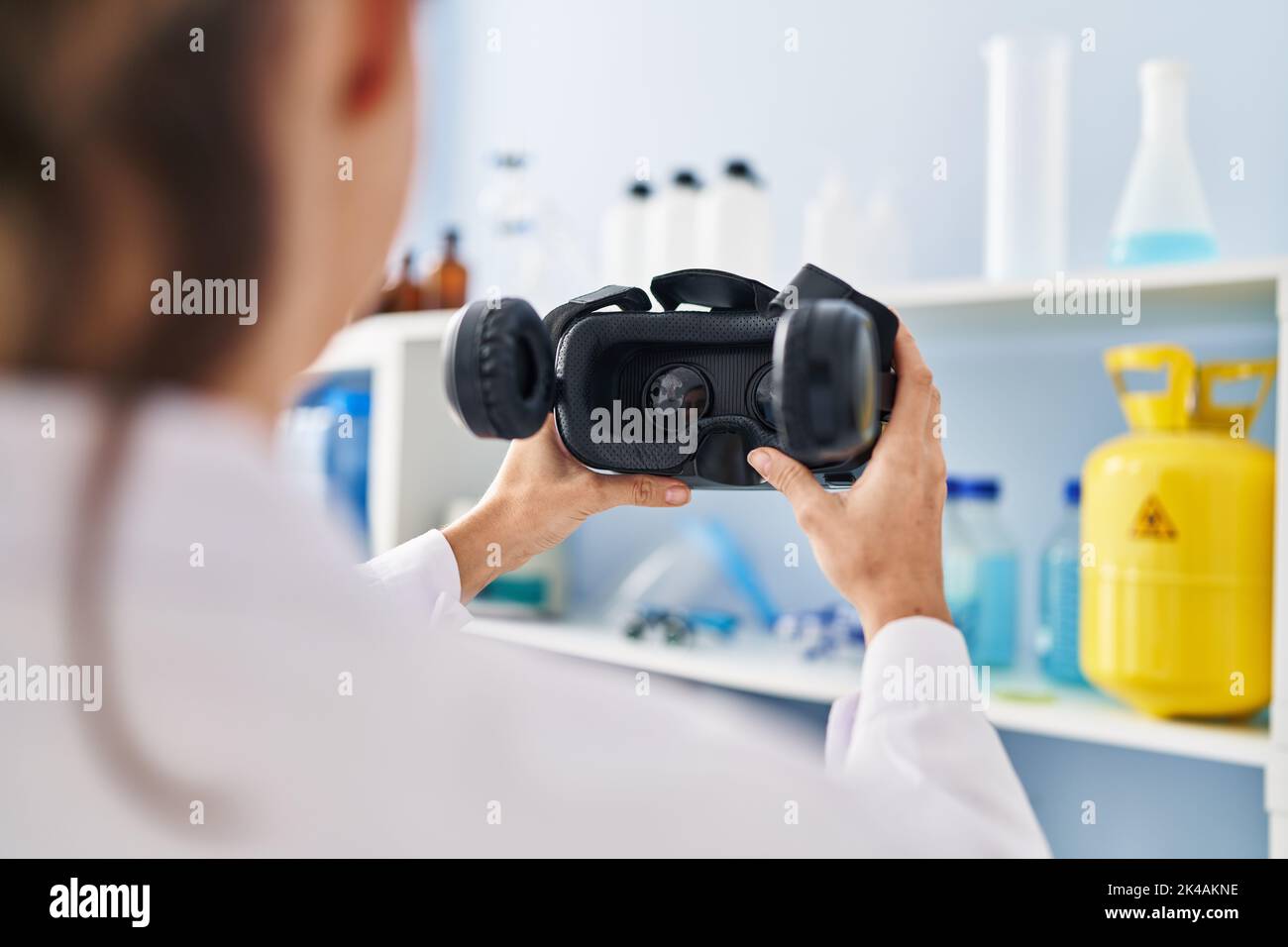 Young woman wearing scientist uniform holding virtual reality goggles ...