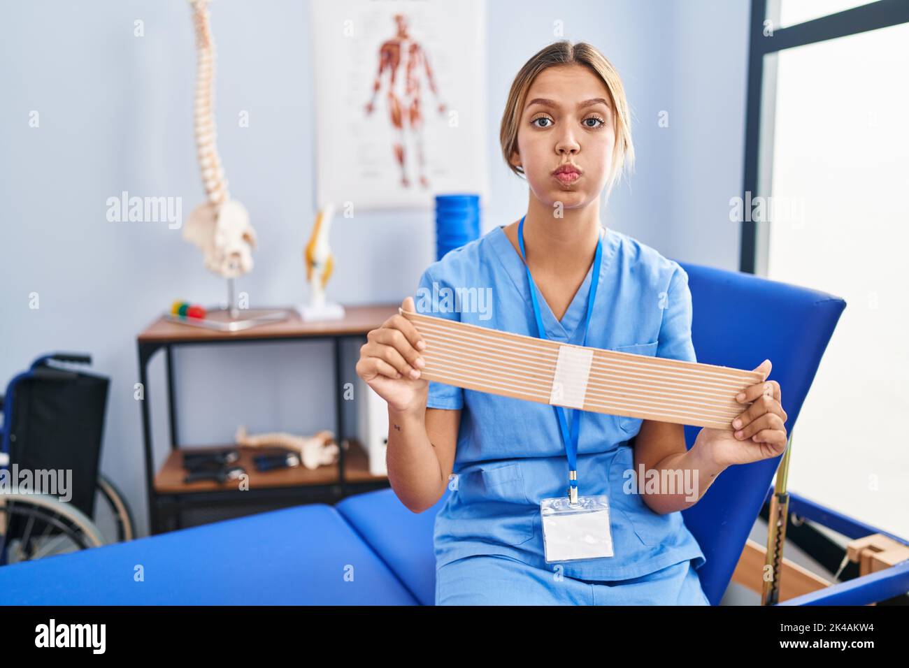Young blonde woman holding therapy corset puffing cheeks with funny ...