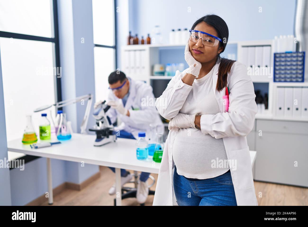 Young hispanic woman expecting a baby working at scientist laboratory ...