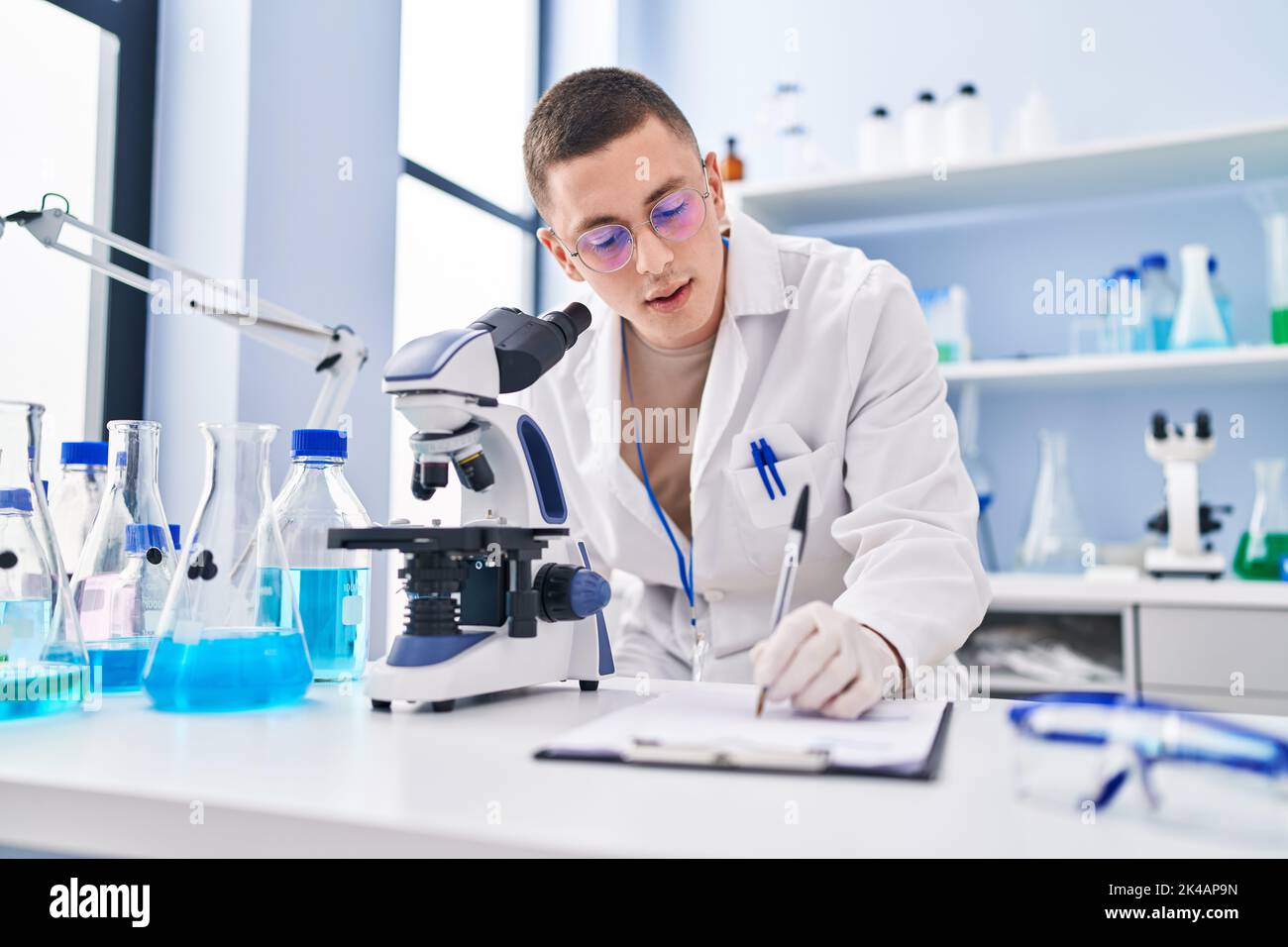 Young hispanic man scientist using microscope writing report at ...