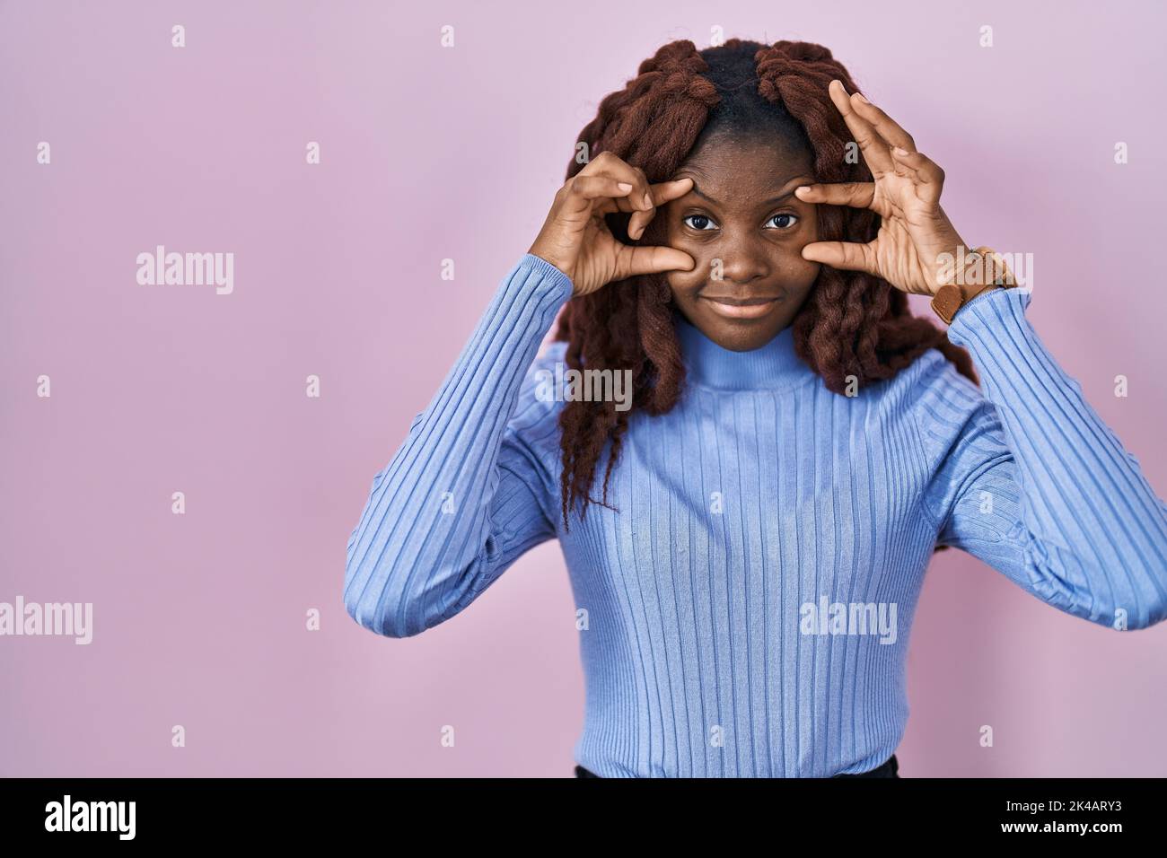 African woman standing over pink background trying to open eyes with ...