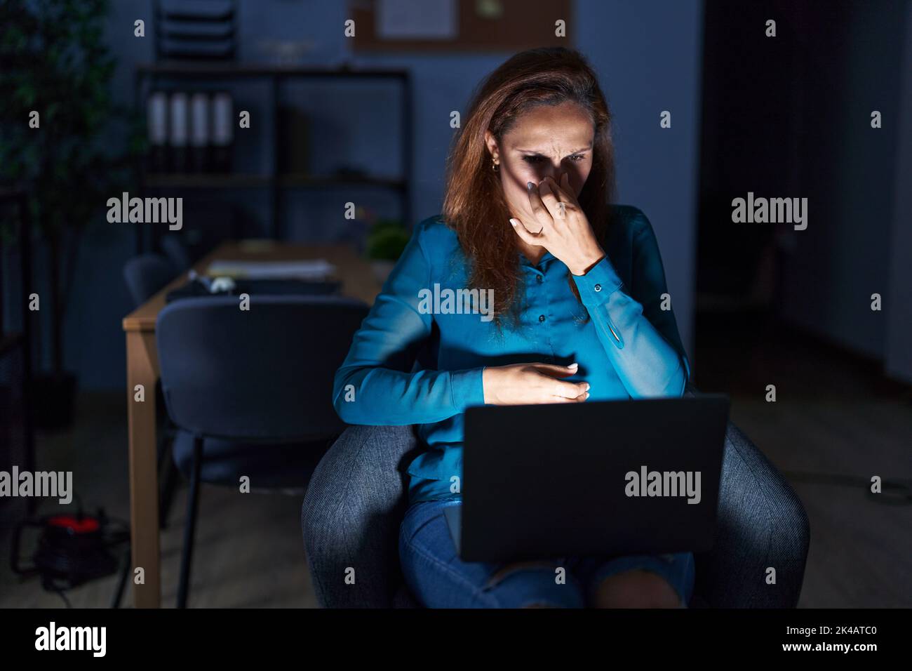 Brunette woman working at the office at night smelling something stinky ...