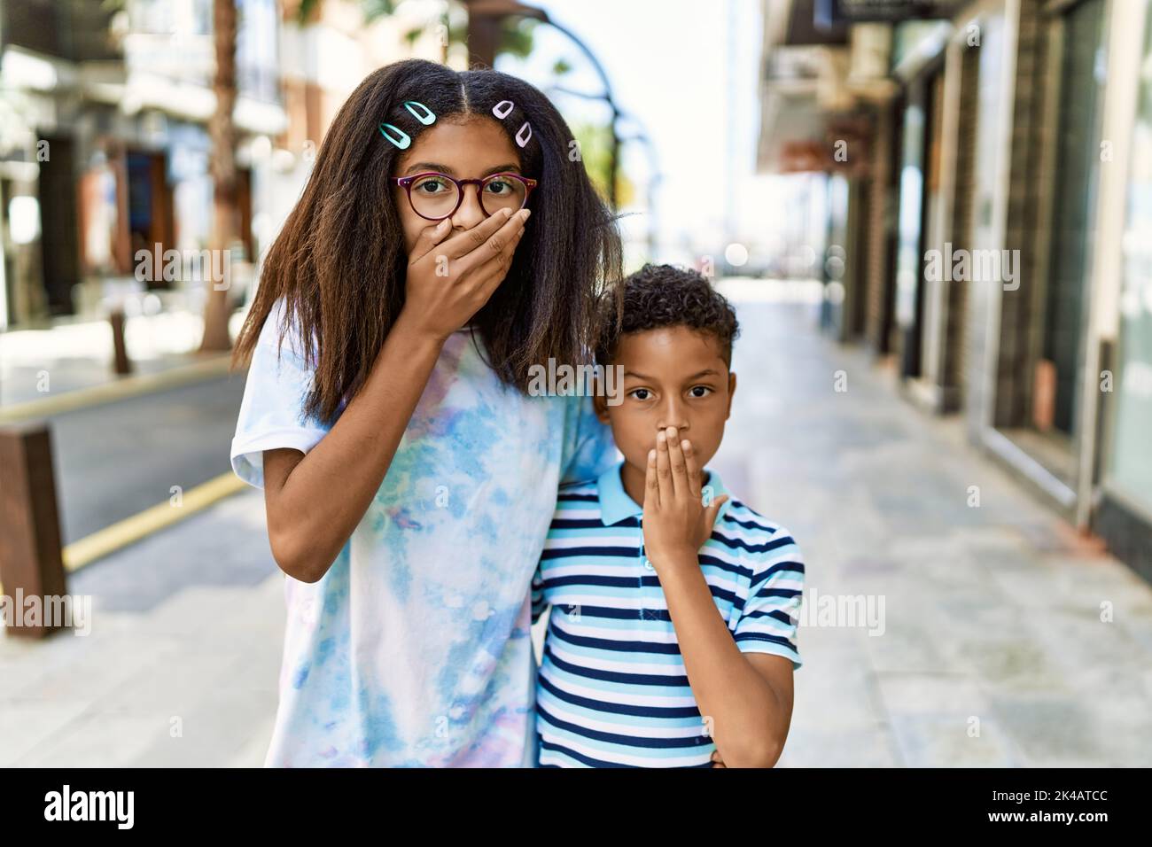 African american family of bother and sister standing at the street covering mouth with hand ...