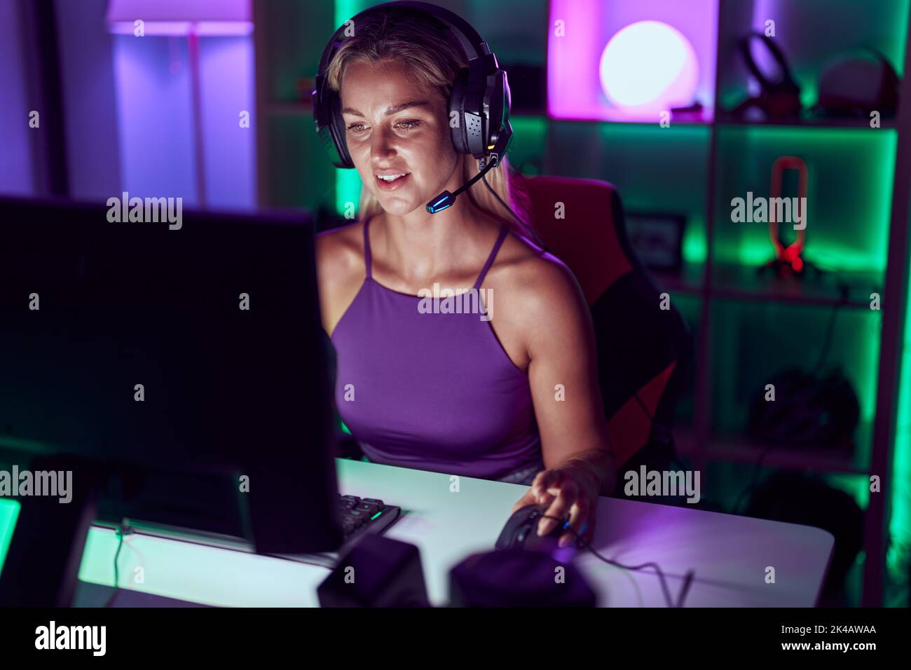 Young blonde woman streamer playing video game using computer at gaming ...
