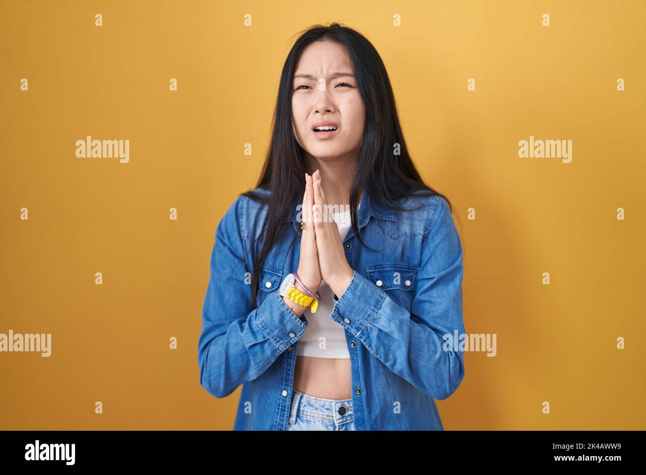 Young asian woman standing over yellow background begging and praying ...