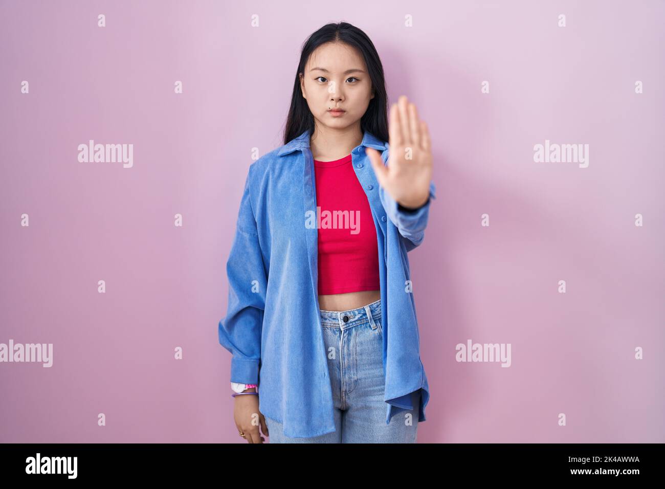Young asian woman standing over pink background doing stop sing with ...