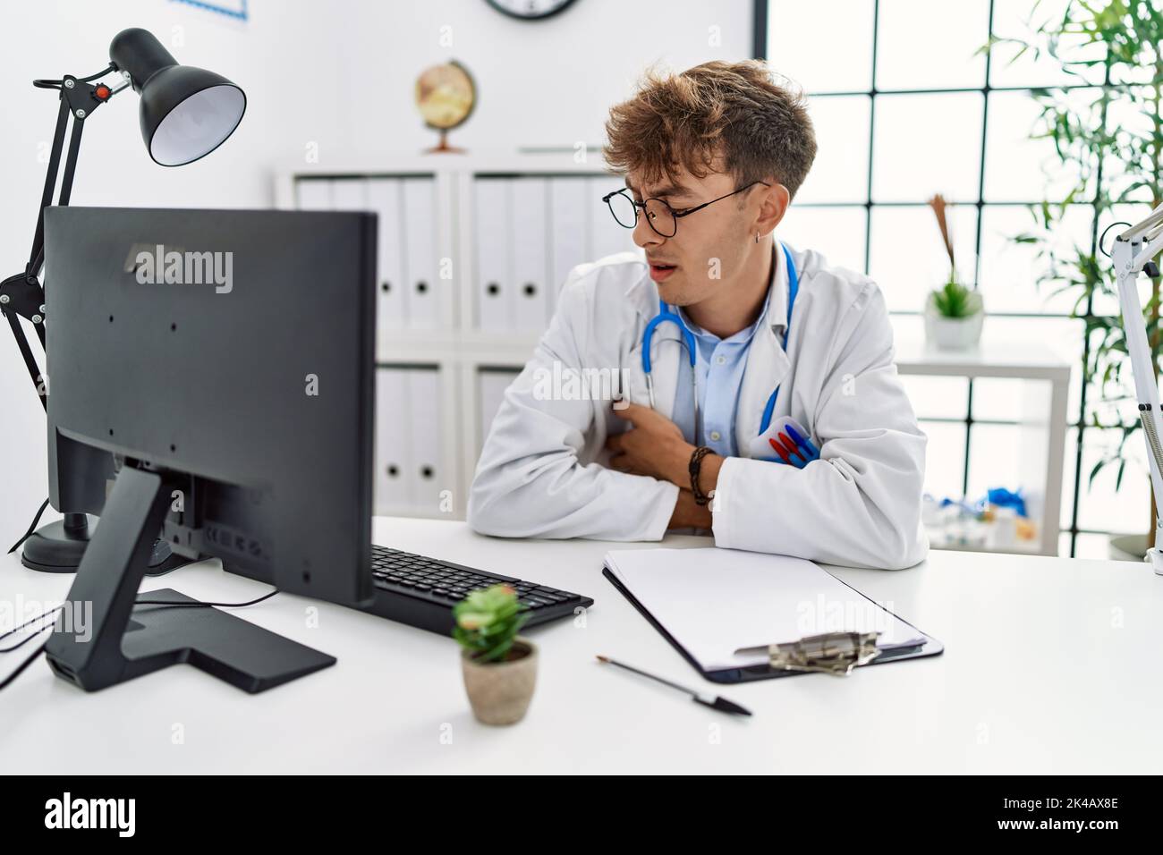 Young caucasian doctor man working at the clinic with hand on stomach ...