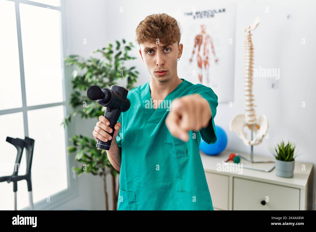 Young caucasian physio man holding muscle percusion gun at the clinic ...