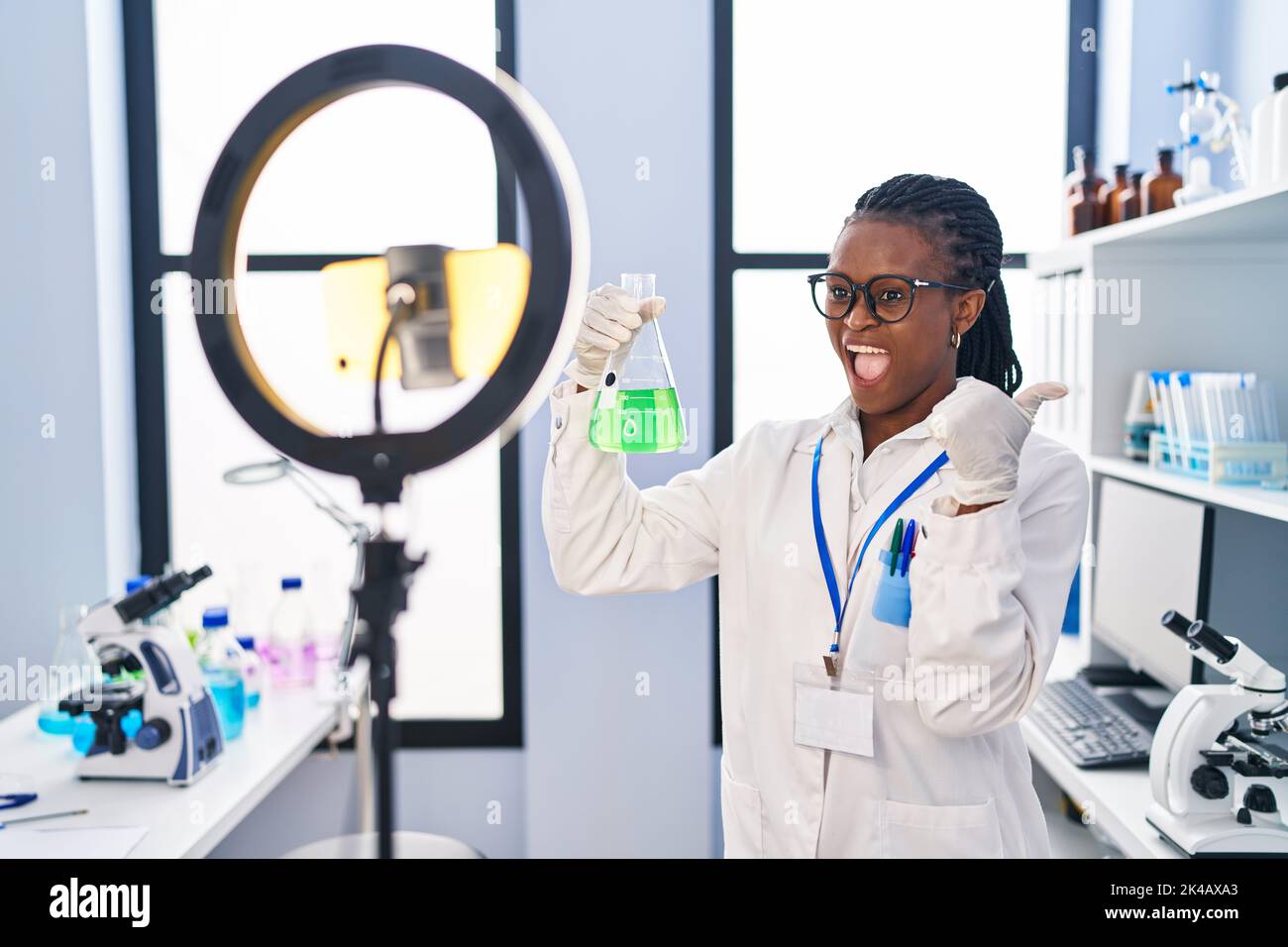 African woman with braids working at scientist laboratory doing tutorial with smartphone ...