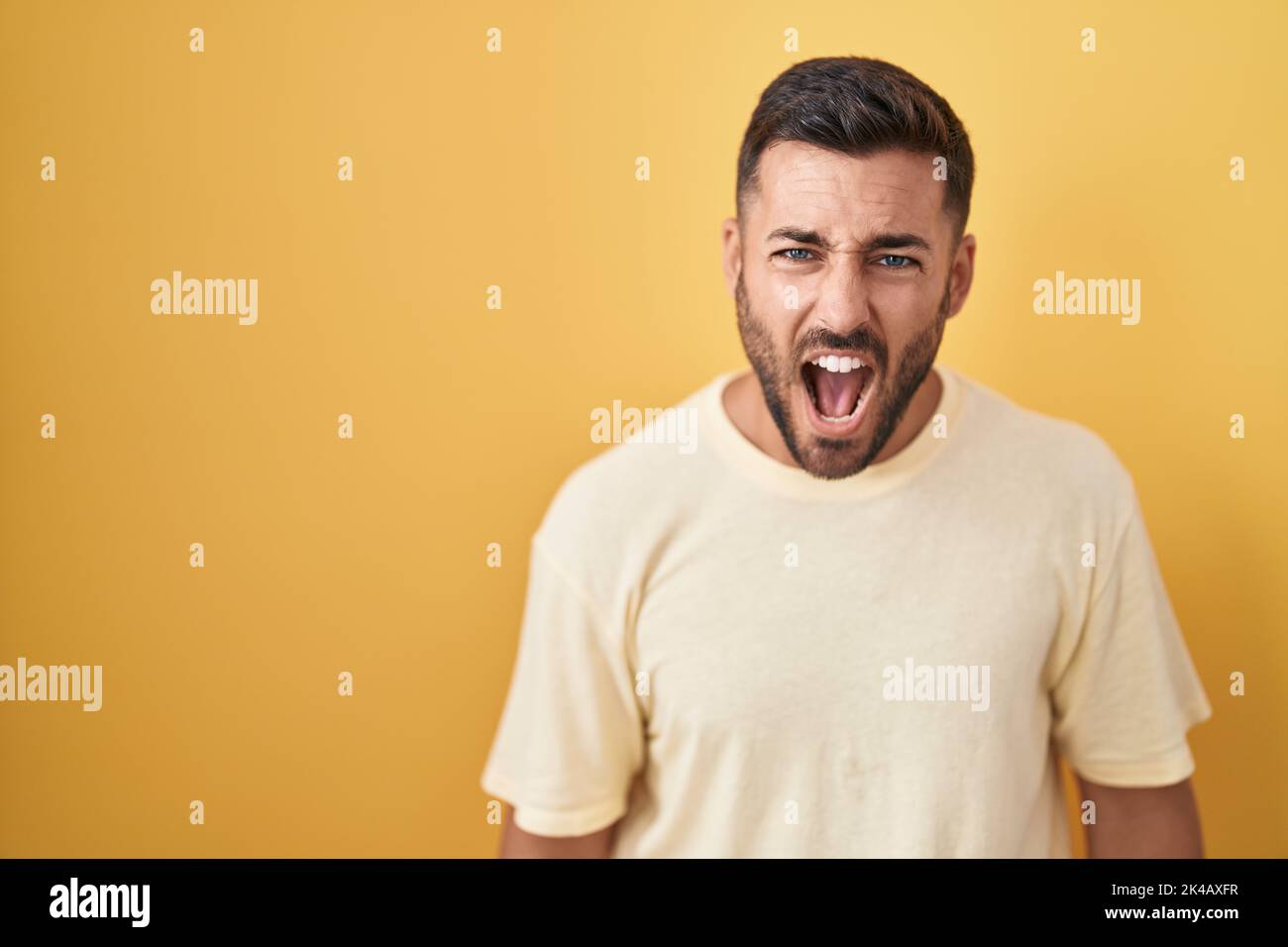 Handsome hispanic man standing over yellow background angry and mad ...