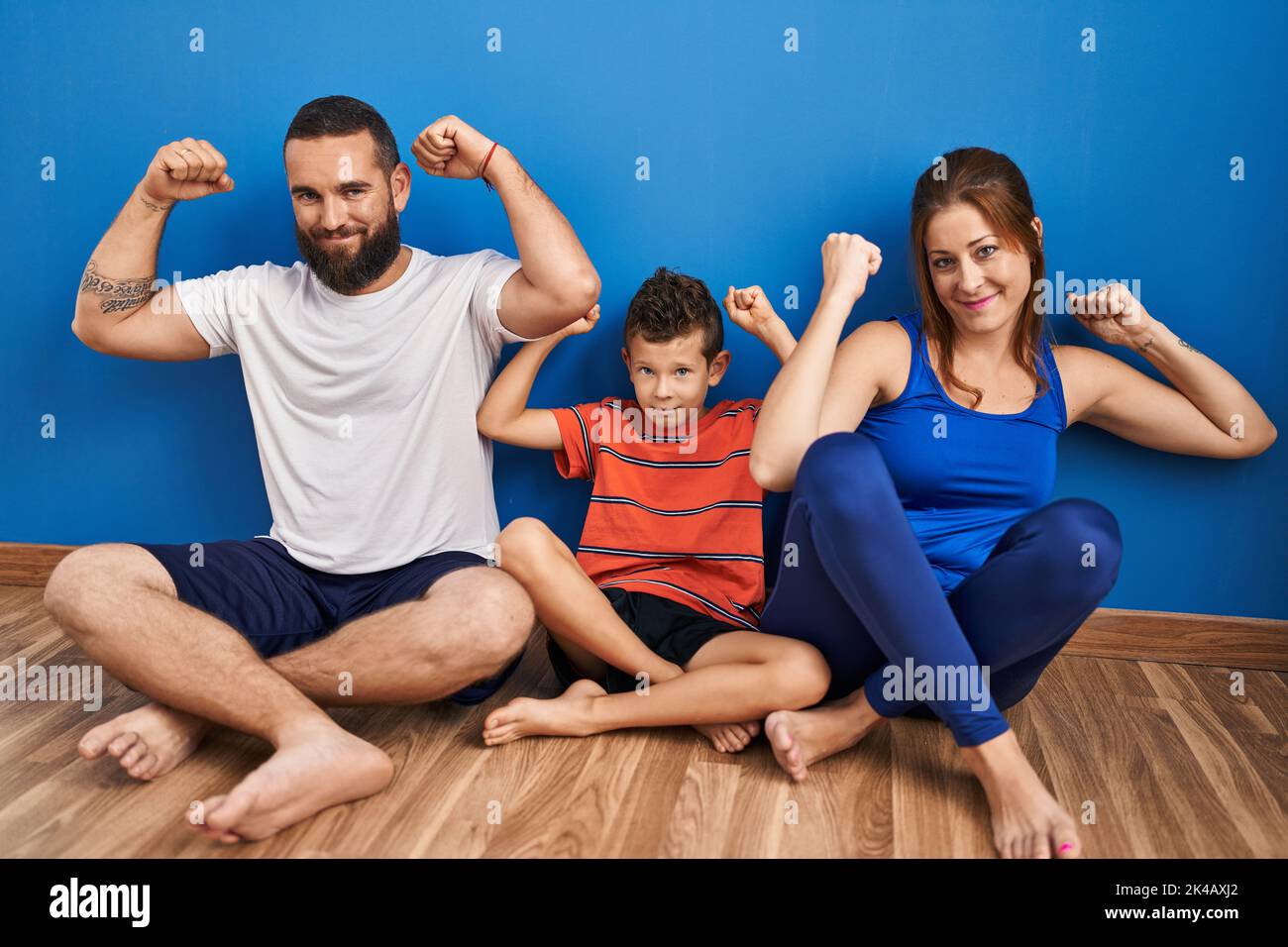 Family of three sitting on the floor at home showing arms muscles ...