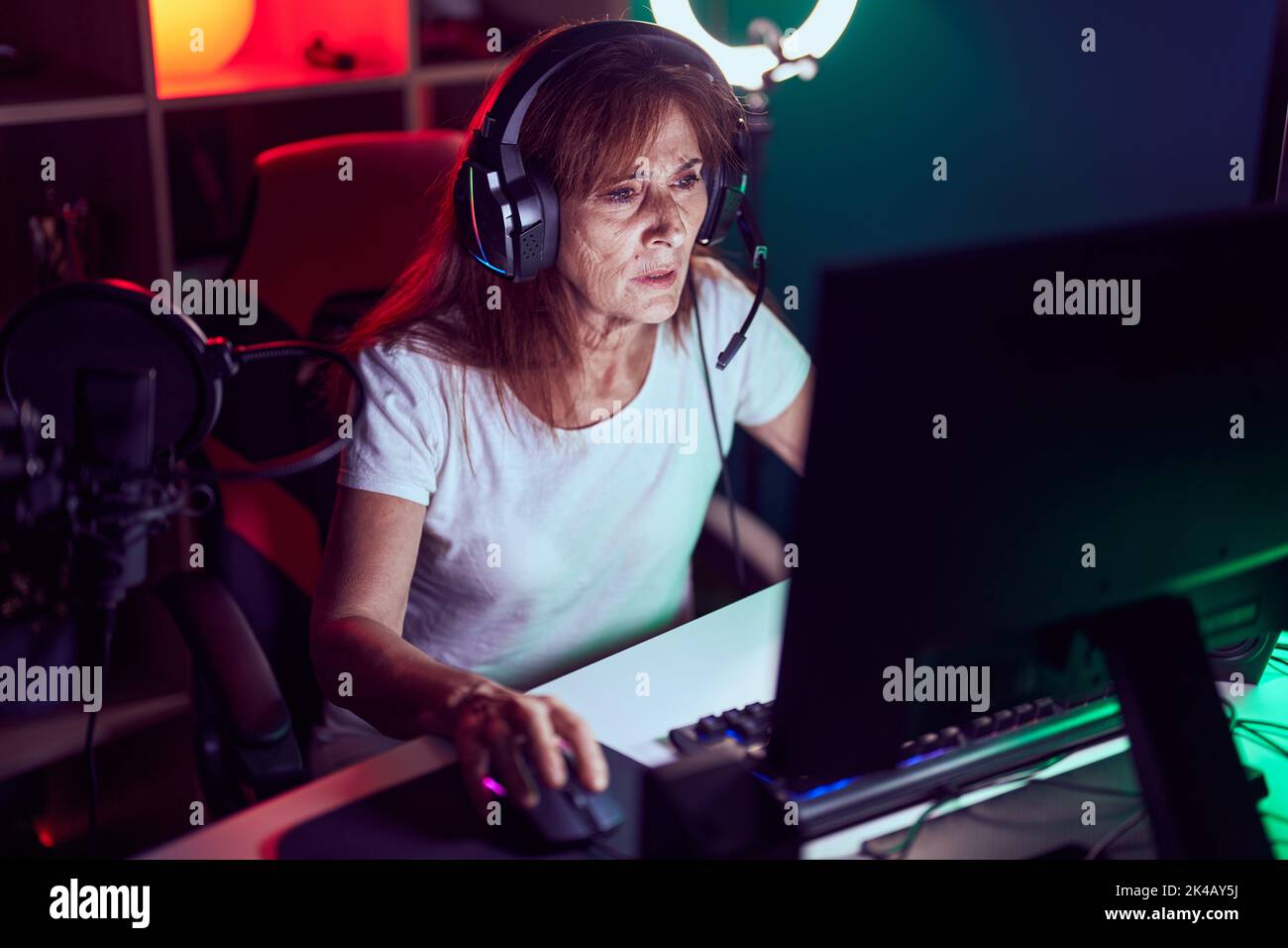 Middle age woman streamer playing video game using computer at gaming ...