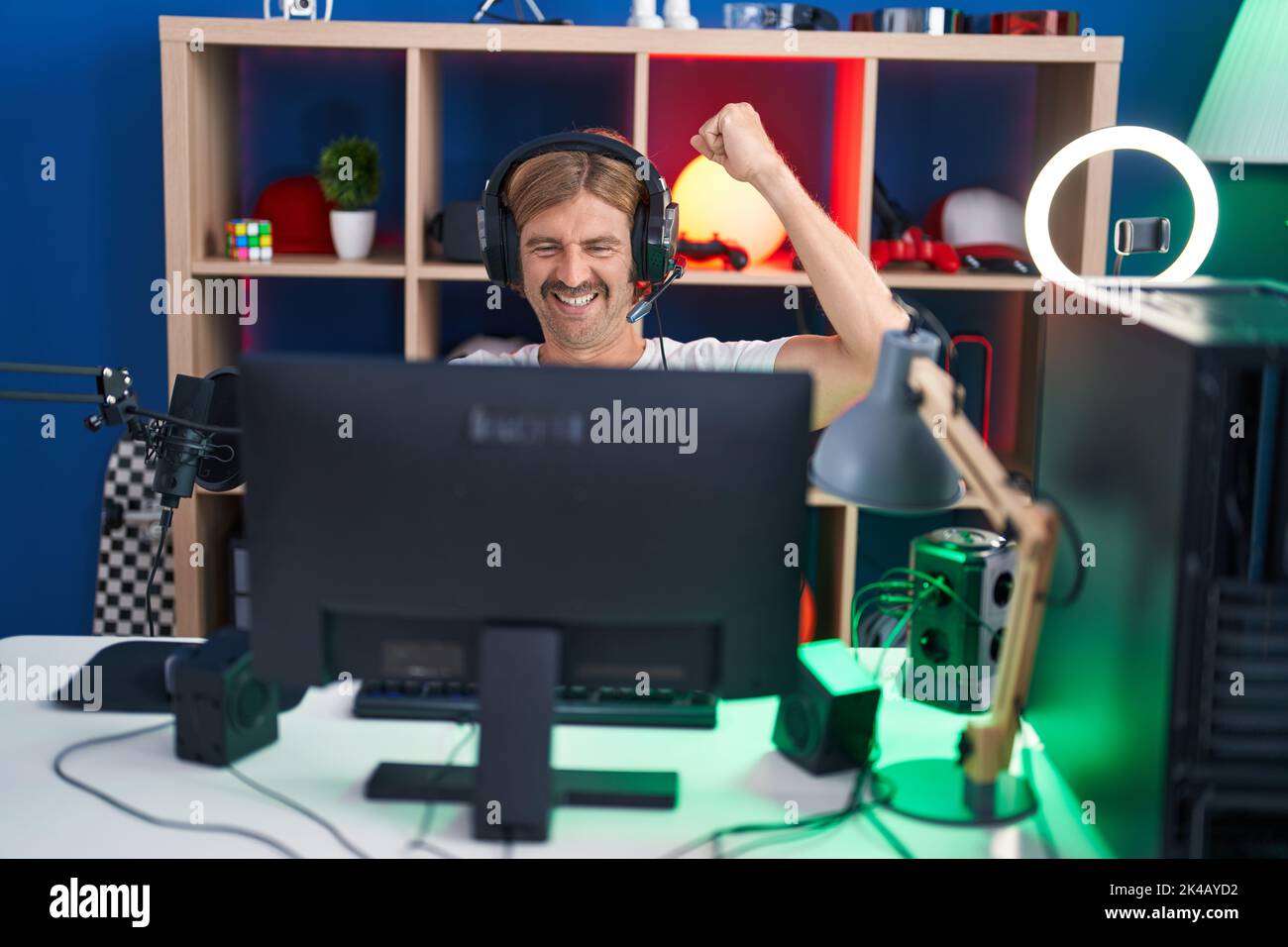 Young blond man streamer playing video game with winner expression at ...