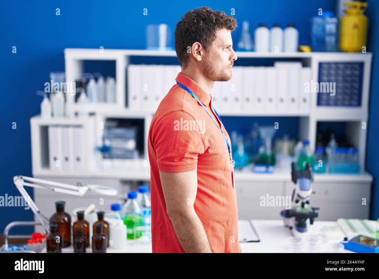 Young hispanic man working at scientist laboratory looking to side, relax profile pose with ...